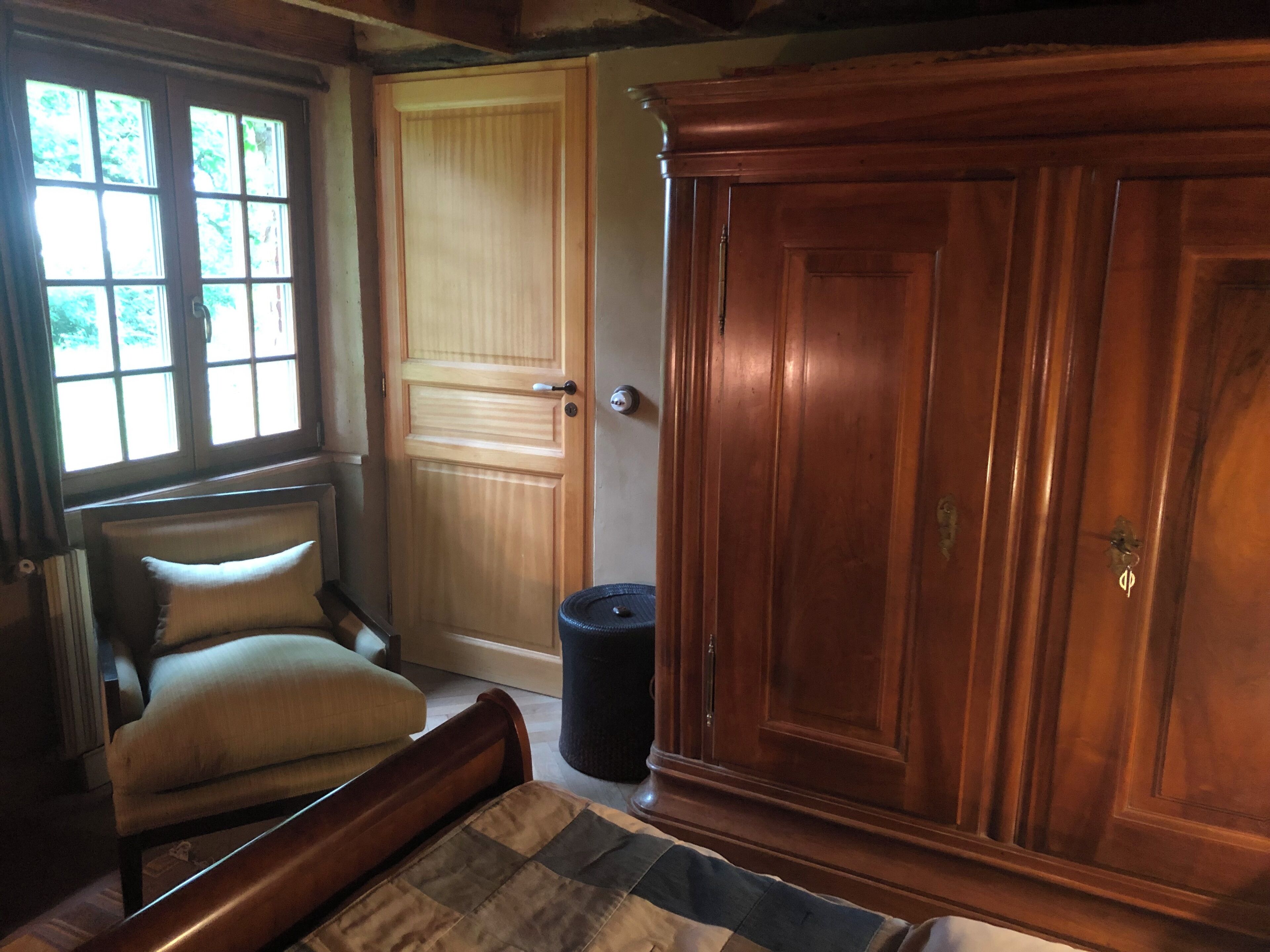 Um quarto com porta de madeira, um banco e um armário grande.