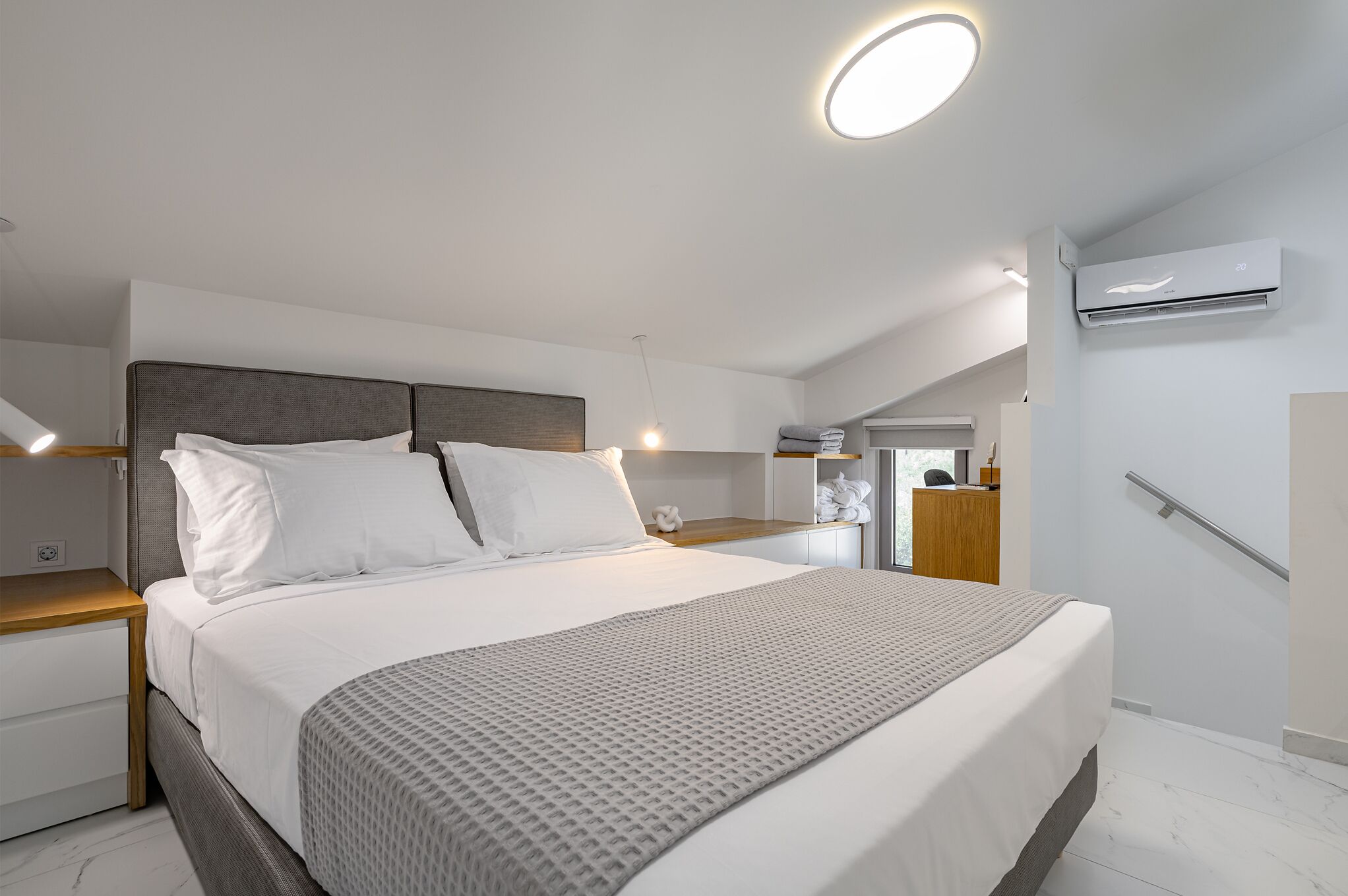 Quarto de hotel moderno com uma cama grande, mesas de cabeceira, guarda-roupa embutido e ar condicionado.
