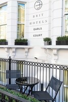 Um edifício branco com a placa 'BRIT HOTELS EARLS COURT' e uma varanda com duas cadeiras e uma mesa.