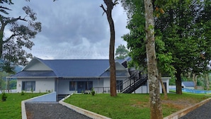 Uma casa moderna com dois andares e telhado azul, cercada por um gramado bem cuidado e árvores.