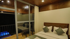Quarto com cama grande, varanda com mesa e cadeiras, e vista para uma piscina.