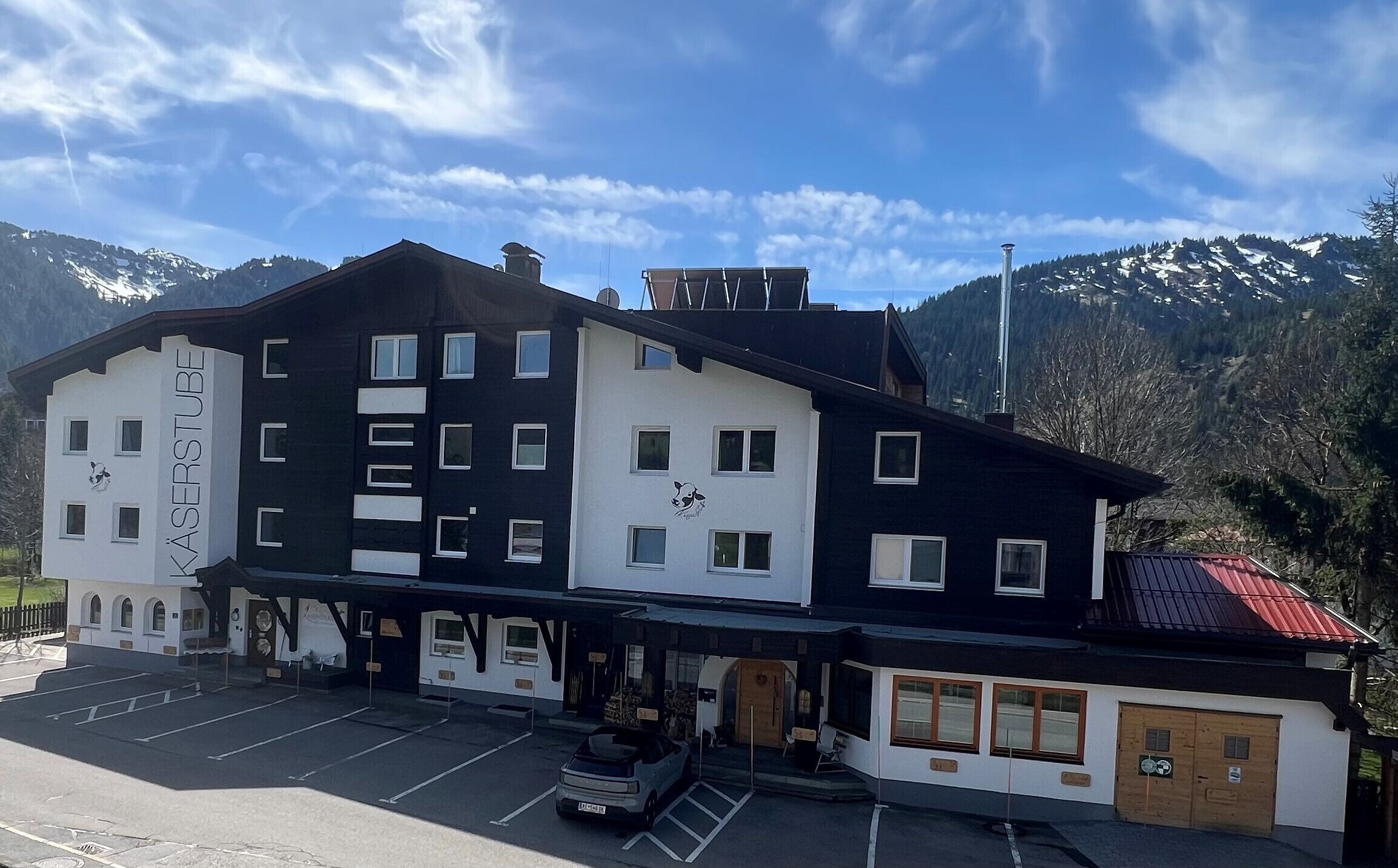 Hotel de vários andares com estacionamento, teleférico e montanhas ao fundo.