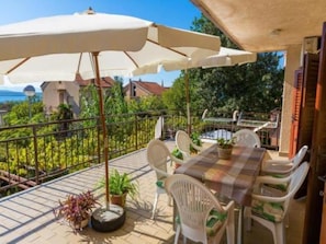 Um terraço com mesa, cadeiras, guarda-sóis e plantas em vasos.