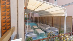 Uma área de estar coberta ao ar livre com piscina, cadeiras acolchoadas e uma mesa.