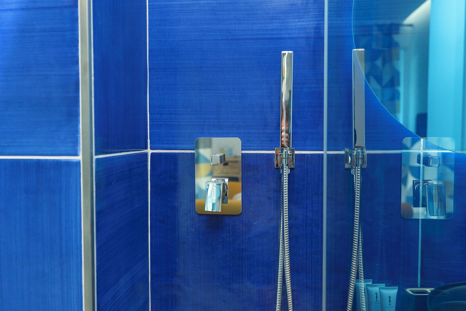 Casa de banho com azulejos azuis, chuveiro com cabeça cromada e mangueira.