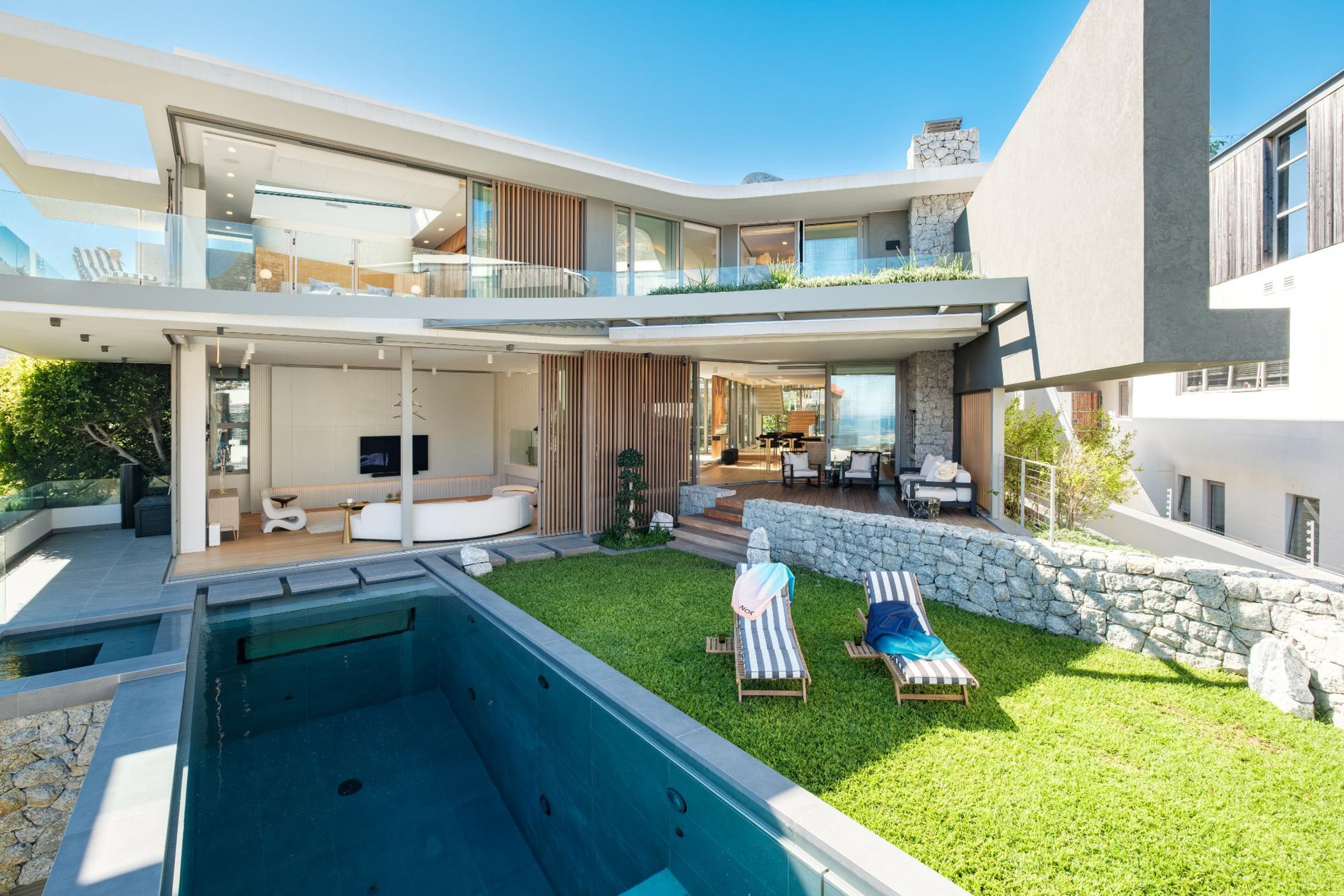 Uma casa moderna de dois andares com piscina, área de estar ao ar livre e muro de pedra.