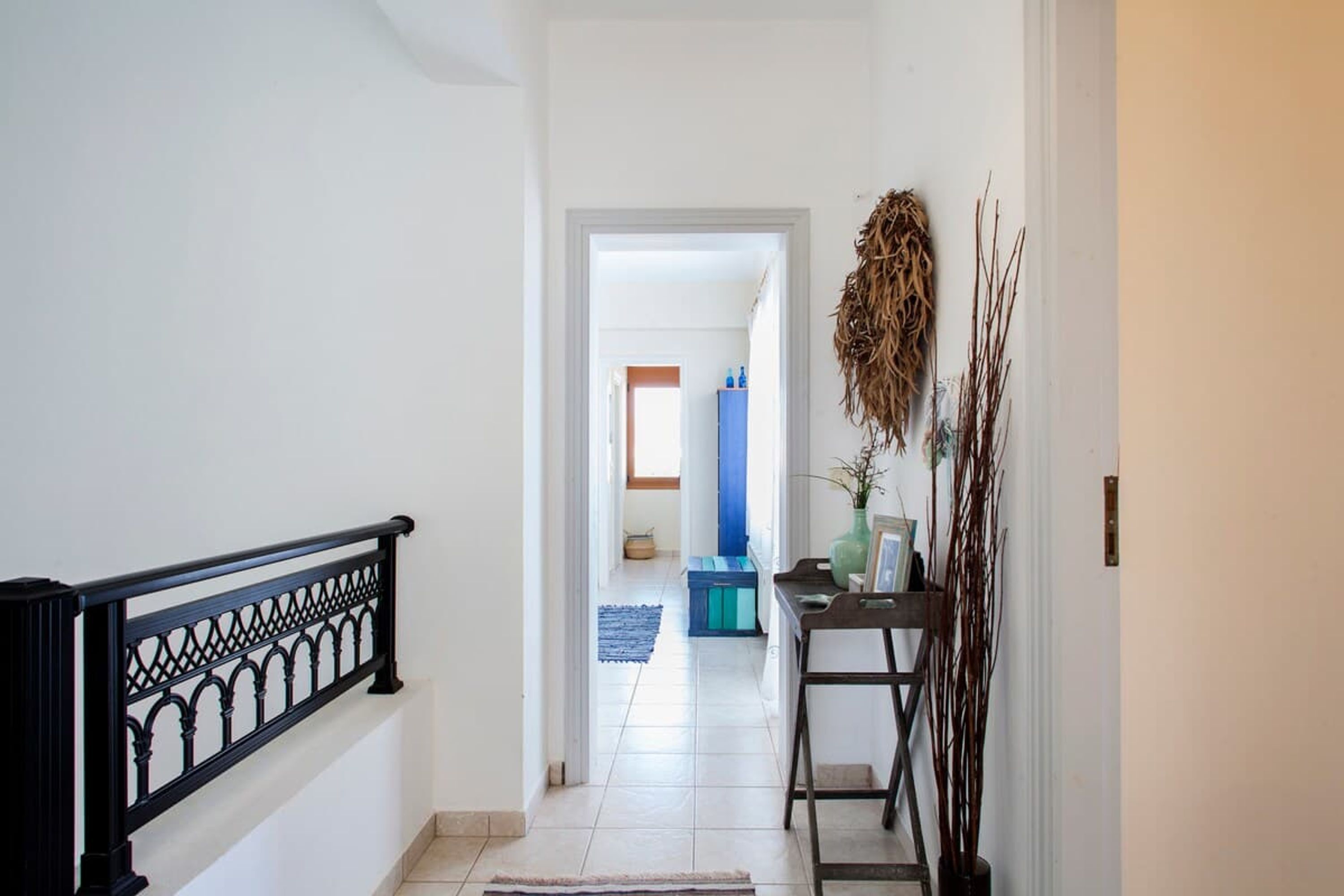 Um corredor com corrimão preto, porta azul e uma pequena mesa com um vaso e galhos.