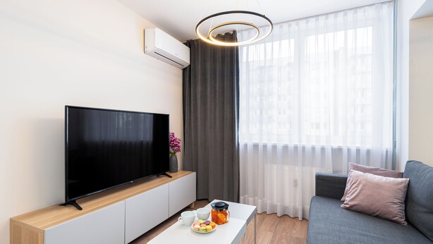 Uma sala de estar moderna com televisão de tela plana, mesa de centro, sofá e uma janela grande com cortinas leves.