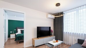 Quarto moderno com cama, televisão, mesa de cabeceira e janela com cortinas.