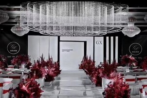 Espaço para eventos formais com lustre, arranjos florais vermelhos e uma placa com a inscrição 'C6X'.