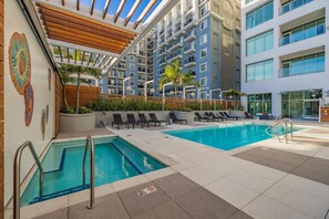 Uma  área de piscina no terraço com espreguiçadeiras, uma pérgola de madeira e vista para edifícios altos.