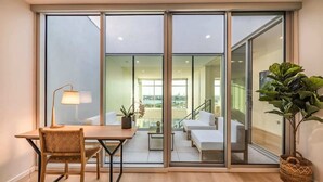 Uma sala de estar moderna com uma porta de vidro que dá para uma varanda, uma área de jantar com mesa e cadeiras, e uma planta grande em vaso.