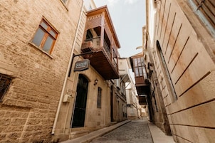 Uma rua de paralelepípedos estreita ladeada por edifícios históricos com varandas e uma placa indicando 'Sazeli Boutique Hotel'.