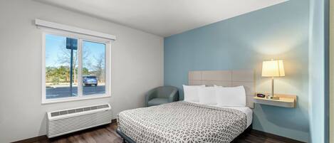 Quarto de hotel moderno com uma cama grande, janela com vista para a rua, aquecedor portátil e mesa de cabeceira com abajur.