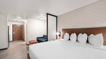Quarto de hotel com uma cama grande, uma cadeira azul, cabeceira de madeira e parede com padrão geométrico.