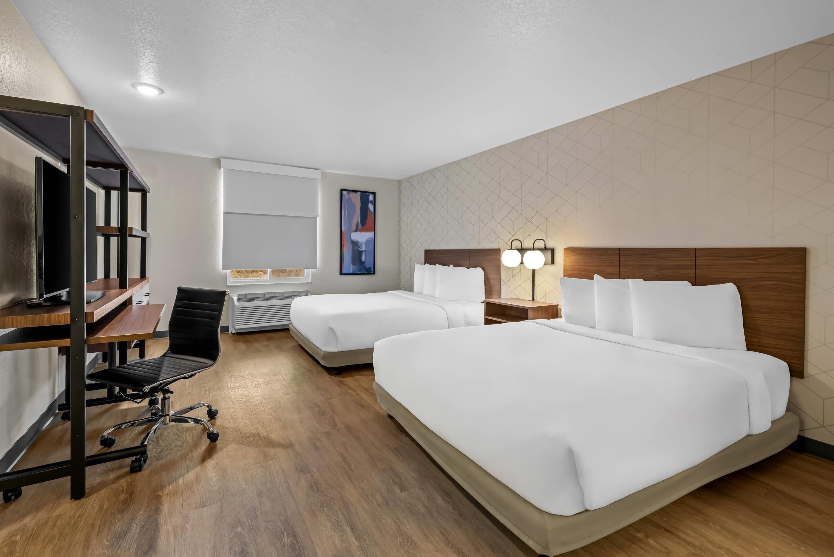 Quarto de hotel com duas camas, uma escrivaninha, uma cadeira e uma televisão.