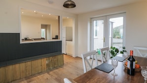Uma cozinha moderna com um banco de madeira, uma mesa de jantar com cadeiras e vista pela porta de vidro.