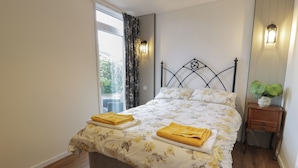 Quarto com cama, mesa de cabeceira, planta em vaso e janela com cortinas.