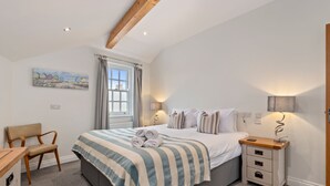 Quarto com cama, mesas de cabeceira, uma cadeira e uma janela com cortinas.