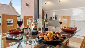 Uma mesa de jantar com frutos do mar, copos de vinho e garrafas, numa cozinha moderna com vista para o exterior.