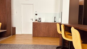 Cozinha moderna com bancada de madeira, máquina de café e pia. Há duas cadeiras amarelas e um banco de madeira na área de jantar.
