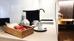 Quarto de hotel moderno com design minimalista, apresentando uma máquina de café, chá e uma caixa de madeira com objetos.