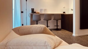 Quarto de hotel moderno com sofá, escrivaninha com computador e área de bar com banquetas.