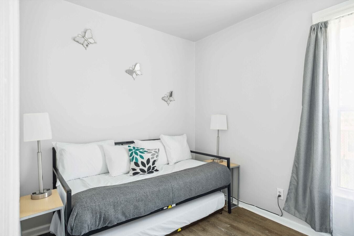 Quarto minimalista com uma cama, duas mesas de cabeceira e uma janela com cortinas.