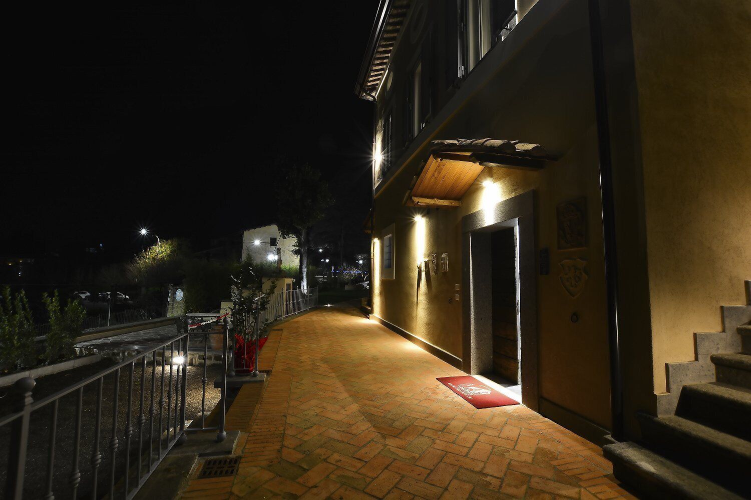 Vista noturna da fachada de um edifício, com um calçada pavimentada que leva a uma porta.