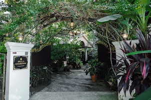Uma entrada com portão para um espaço chamado Bella Homestay, com um caminho de pedras e vegetação exuberante.