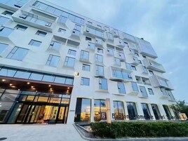 Um hotel moderno com vários andares, grandes janelas e uma entrada imponente com portas de vidro.