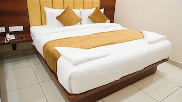 Uma cama bem arrumada com roupa de cama branca e manta marrom, um painel de cabeceira em madeira e uma mesinha de cabeceira com um telefone e controles remotos.