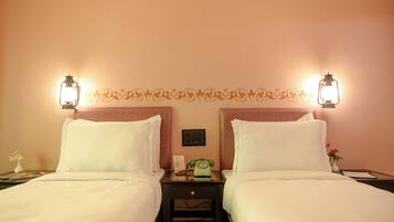Quarto de hotel com duas camas, mesas de cabeceira, telefone e luminárias decorativas na parede.