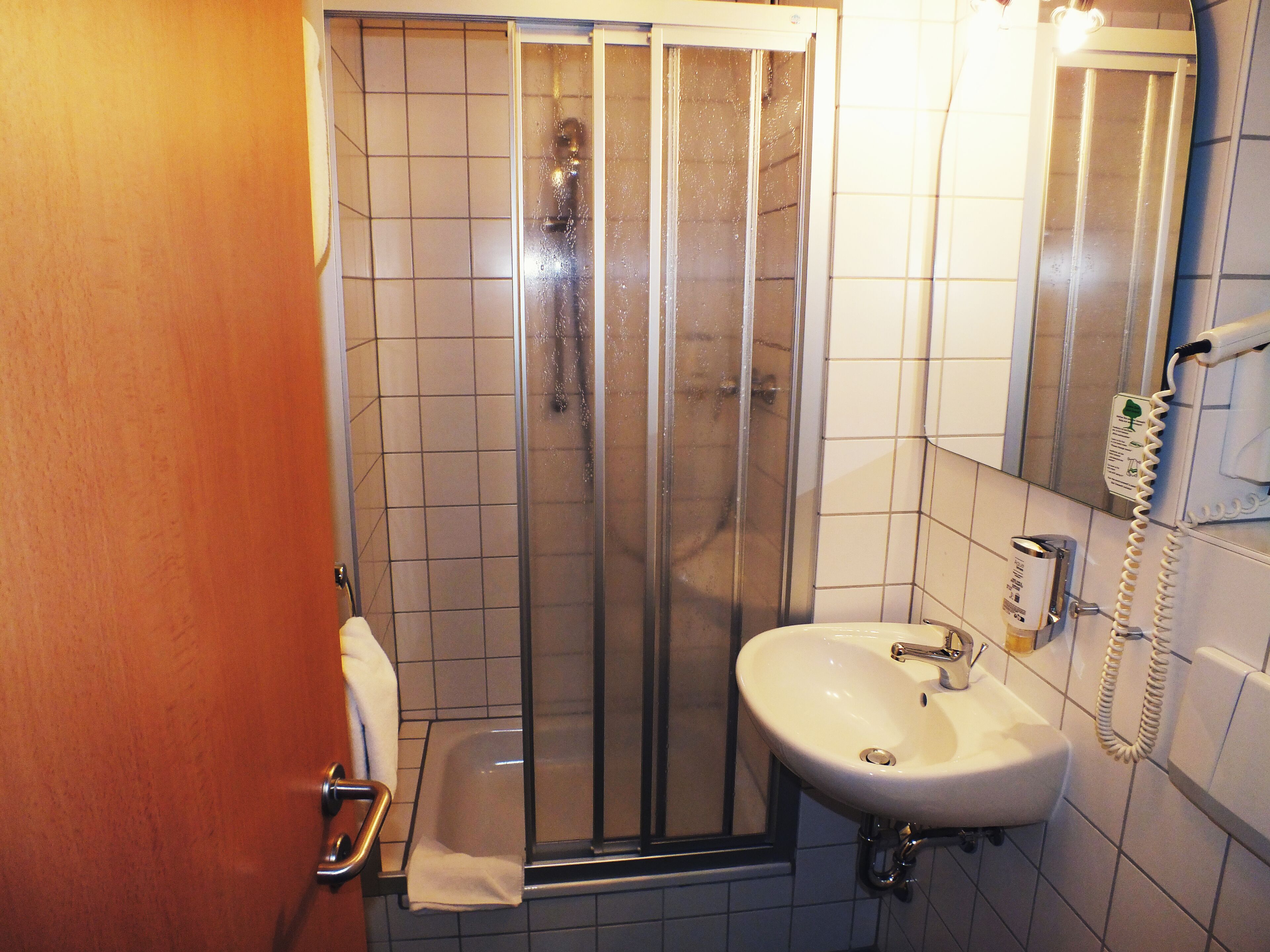 Casa de banho com cabine de duche em vidro, lavatório e telefone.