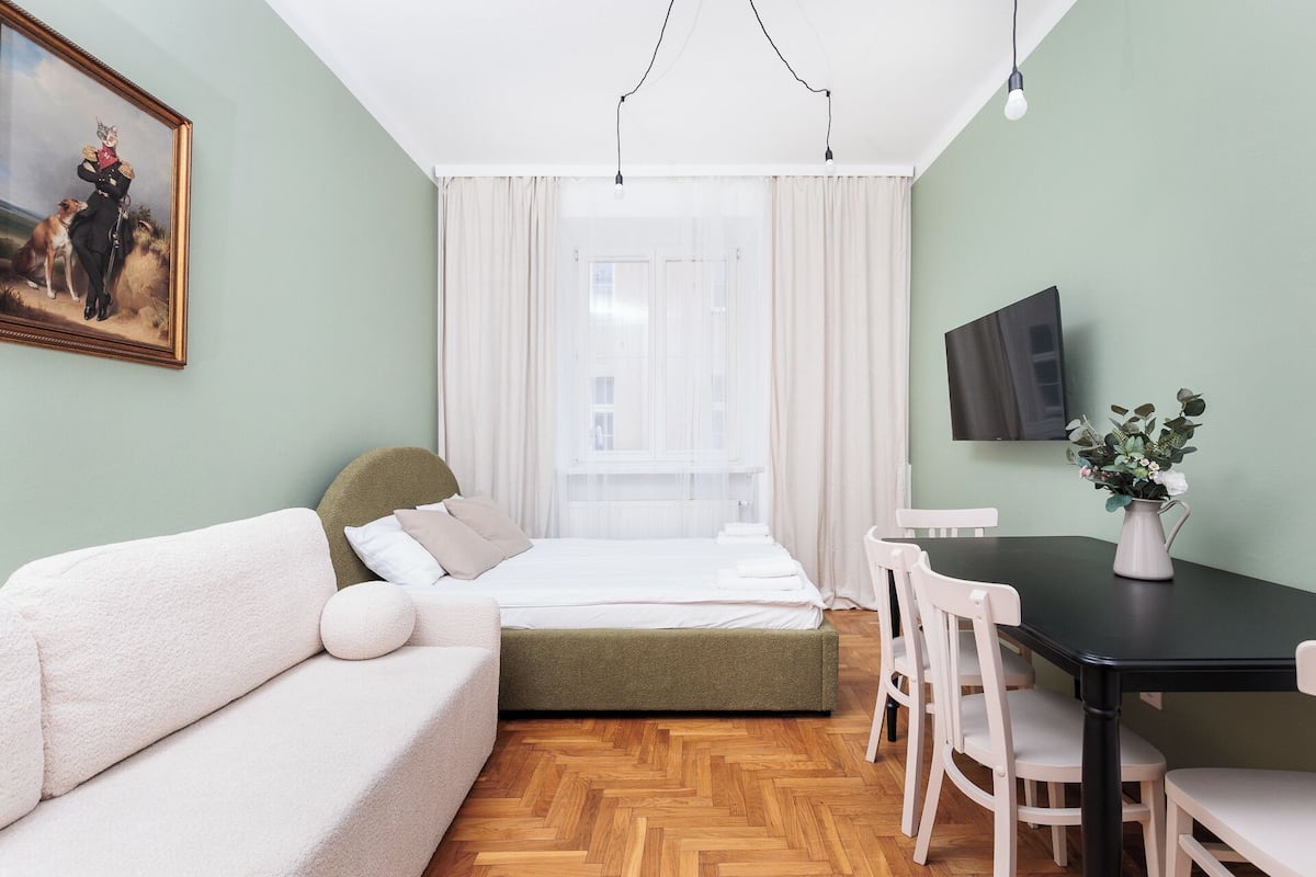 Um quarto aconchegante com uma cama, um sofá, uma mesa de jantar com cadeiras, uma televisão e um quadro na parede.