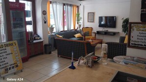 Uma sala de estar com sofá, televisão, máquina de refrigerantes Coca-Cola e placa de bebidas geladas.