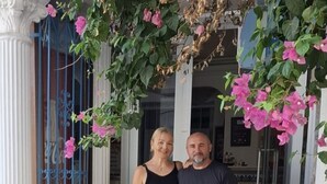 Um casal em uma escadaria de pedra, com um portão de ferro forjado e plantas floridas.