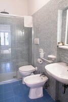Casa de banho com chuveiro, sanita, bidé e lavatório.