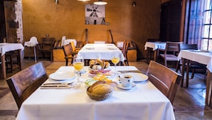 Uma sala de jantar com mesas preparadas para o café da manhã, com pães, doces e frutas.