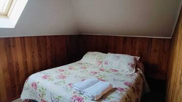 Quarto com teto inclinado, claraboia, colcha florida e tapete estampado.