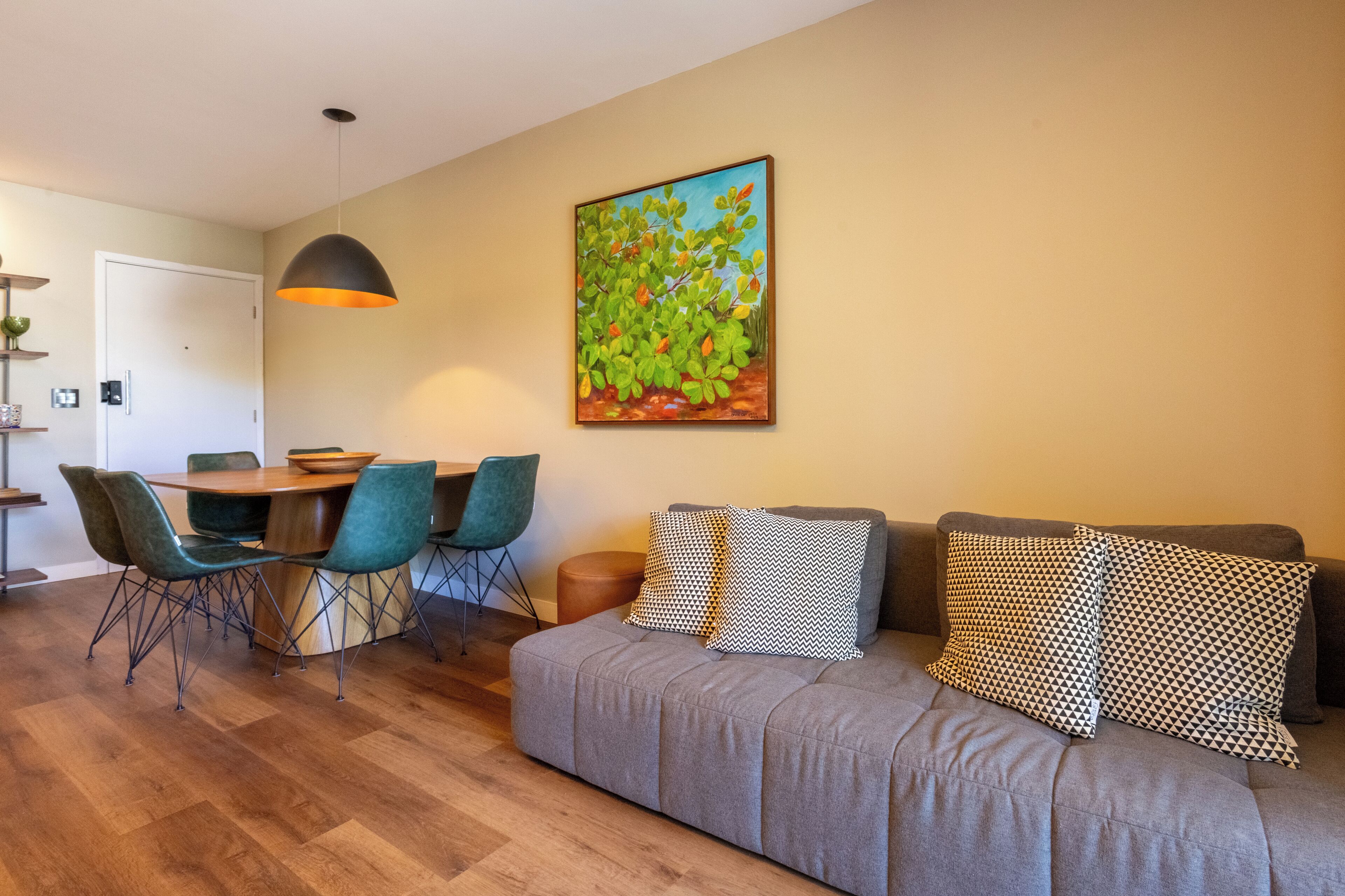 Uma sala de estar moderna com sofá cinza, cadeiras verde-água, mesa de jantar de madeira e luminária pendente.