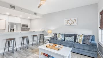 Um espaço de estar moderno com cozinha, banquetas de bar, sofá com almofadas e mesa de centro.