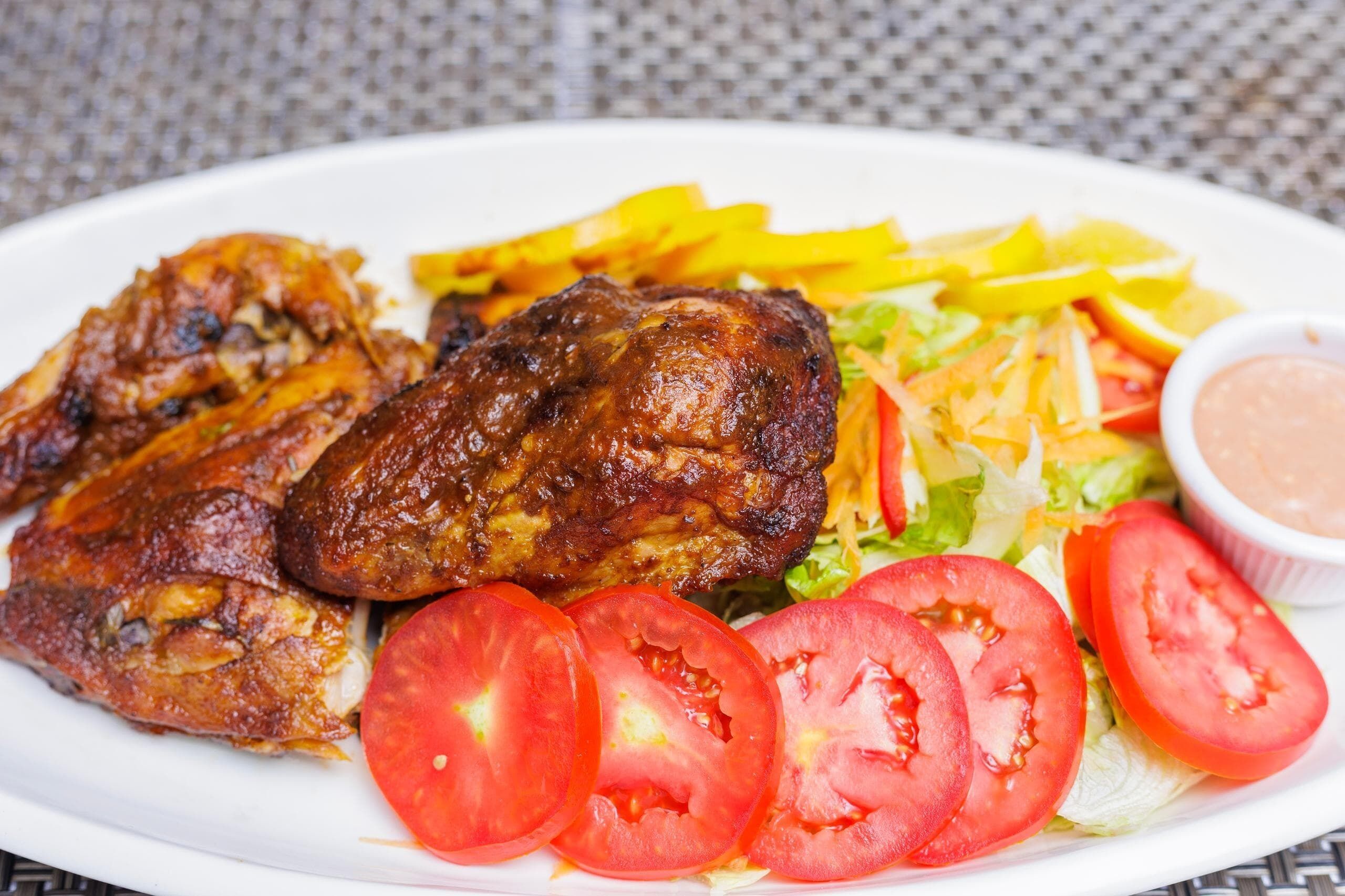 Um prato de frango grelhado, tomates fatiados e uma salada com molho para acompanhar.