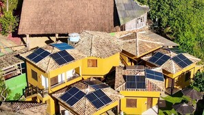 Um conjunto de edifícios amarelos com painéis solares nos telhados, cercado por vegetação exuberante.
