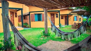 Um pátio com uma rede, uma pérgola de madeira e uma pequena mesa com guarda-sol.