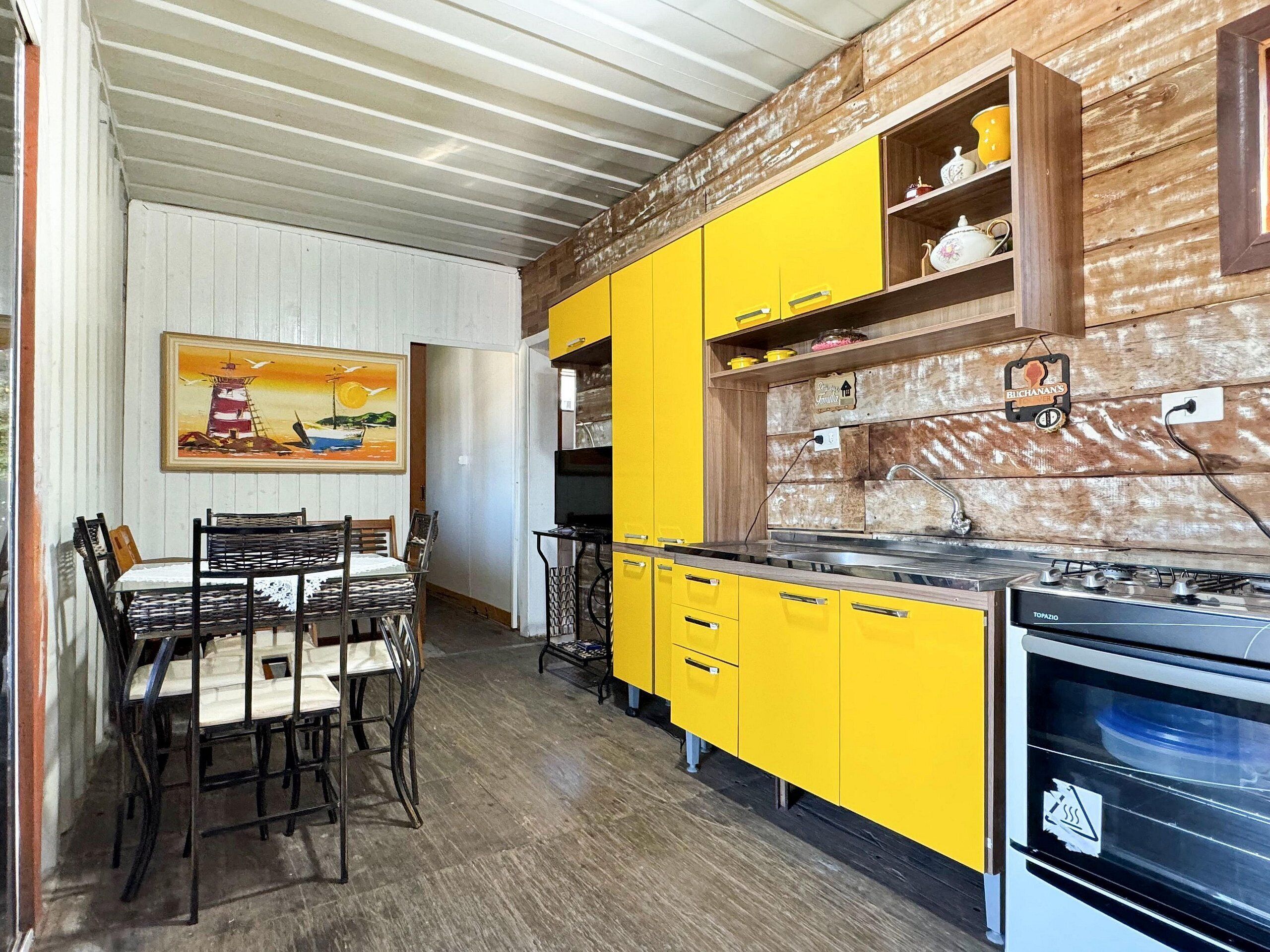 Uma cozinha com armários amarelos, painel de fundo de madeira e uma pintura de um farol.