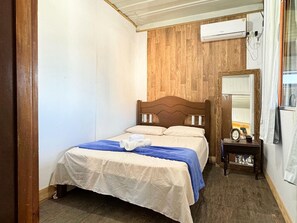 Uma cama de solteiro com cabeceira de madeira, mesa de cabeceira com relógio e unidade de ar condicionado na parede.