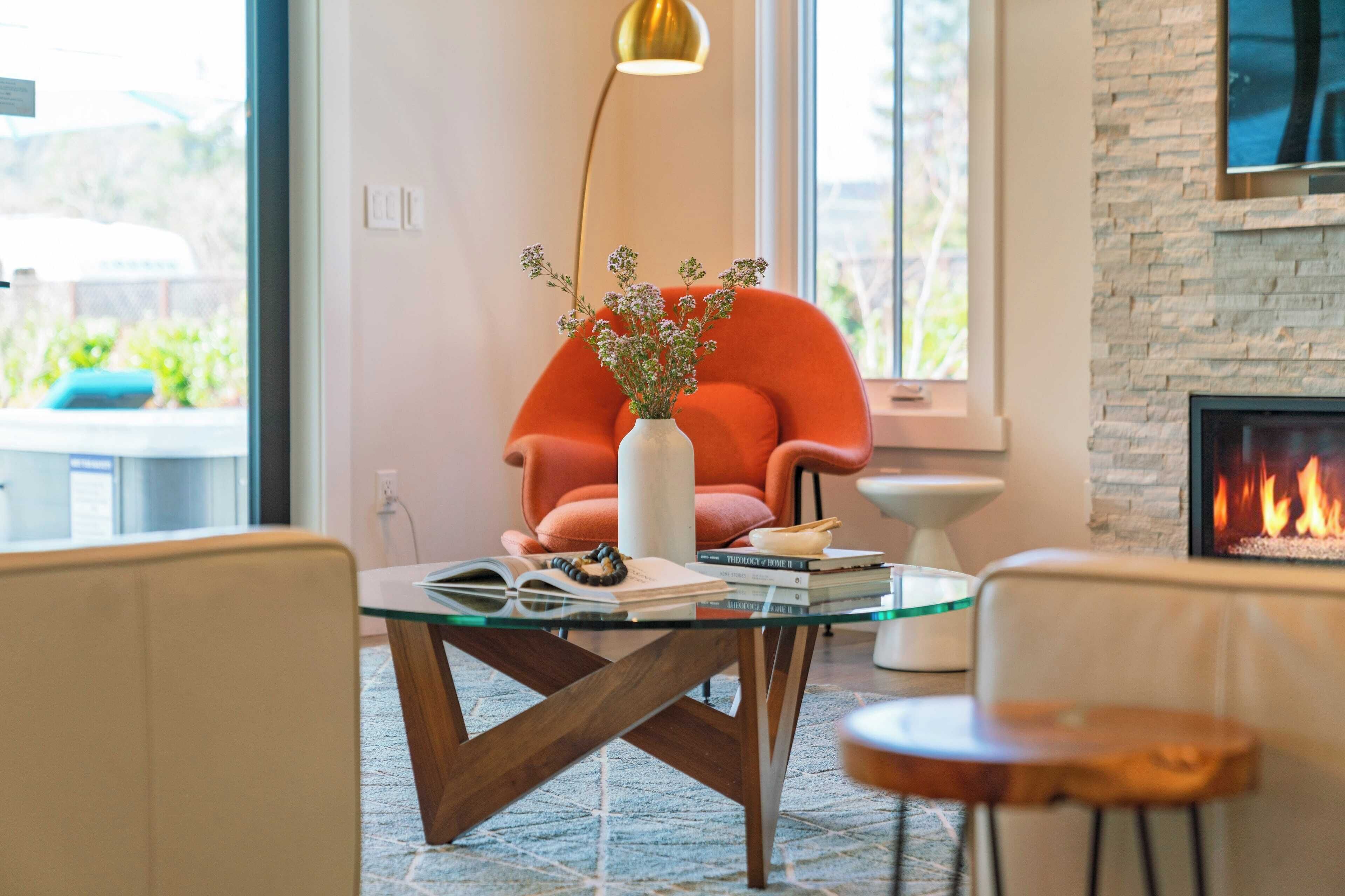 Uma sala de estar moderna com uma mesa de centro de vidro, uma poltrona vermelha e uma lareira.