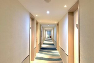 Corredor de hotel com carpete listrado, portas em ambos os lados e teto de cor clara.