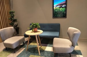 Quarto com sofá, duas poltronas, uma mesa redonda pequena com uma planta e um quadro na parede.